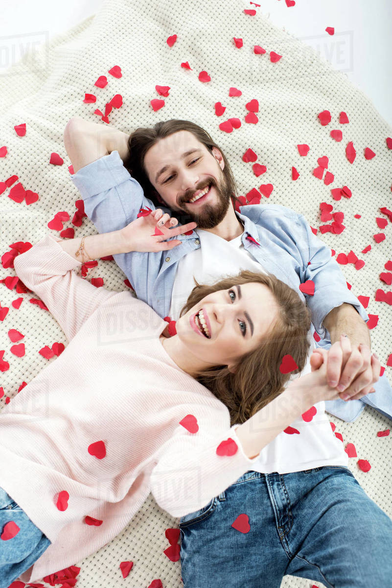 Beautiful young couple in love lying together and smiling on red paper ...