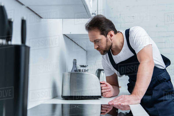 serious handyman in working overall fixing toaster in kitchen - Royalty ...