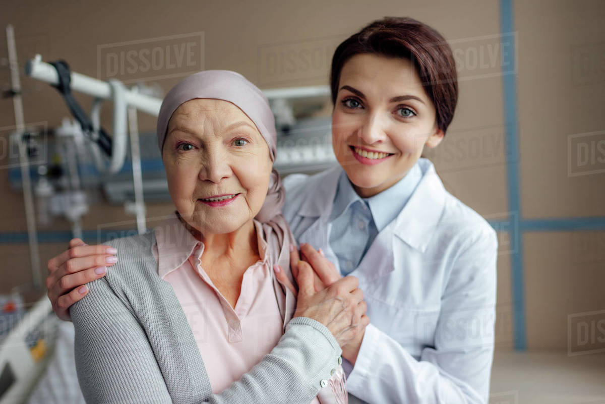 Happy female doctor hugging senior woman in kerchief with cancer and ...