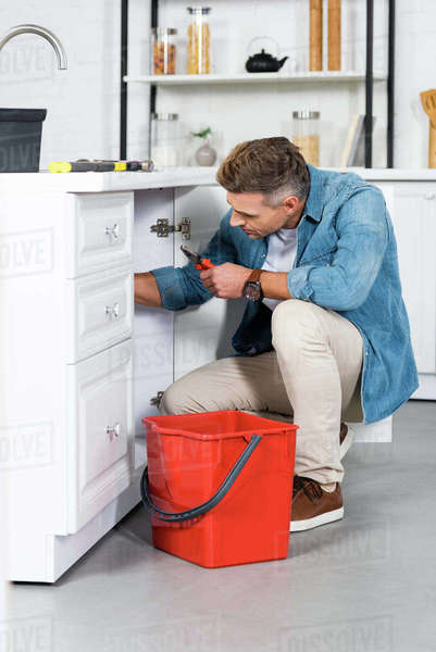 Handsome adult man repairing kitchen sink - Stock Photo - Dissolve