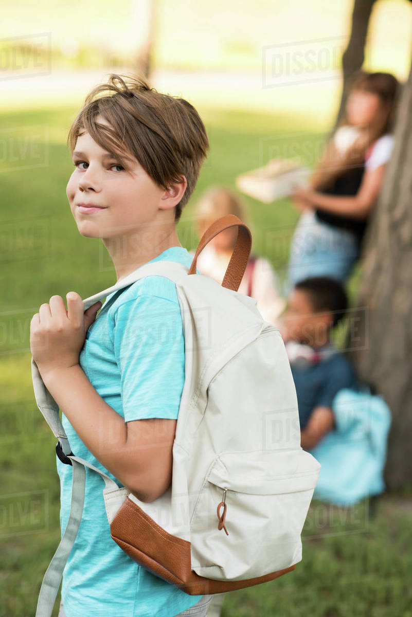 Portrait of smiling teenage boy holding backpack and looking at camera ...
