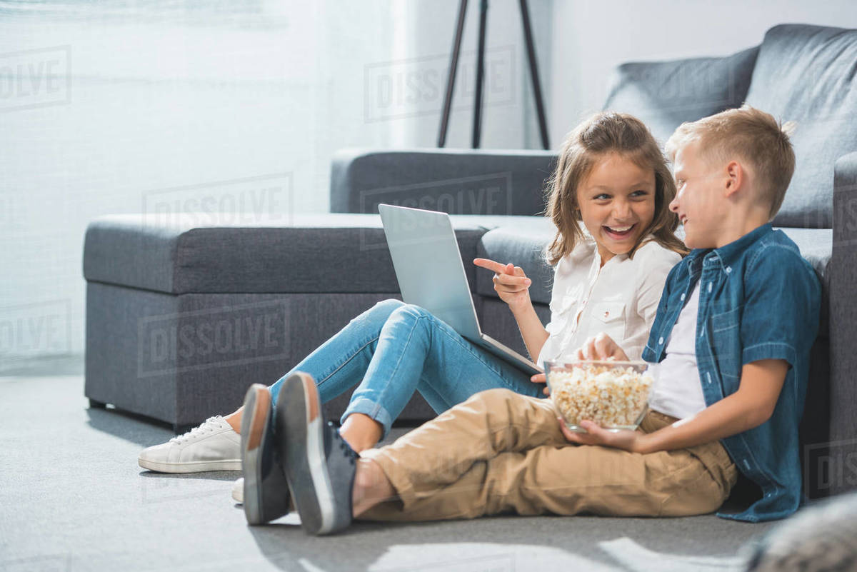 Smiling children using laptop and eating popcorn at home - Royalty-free ...