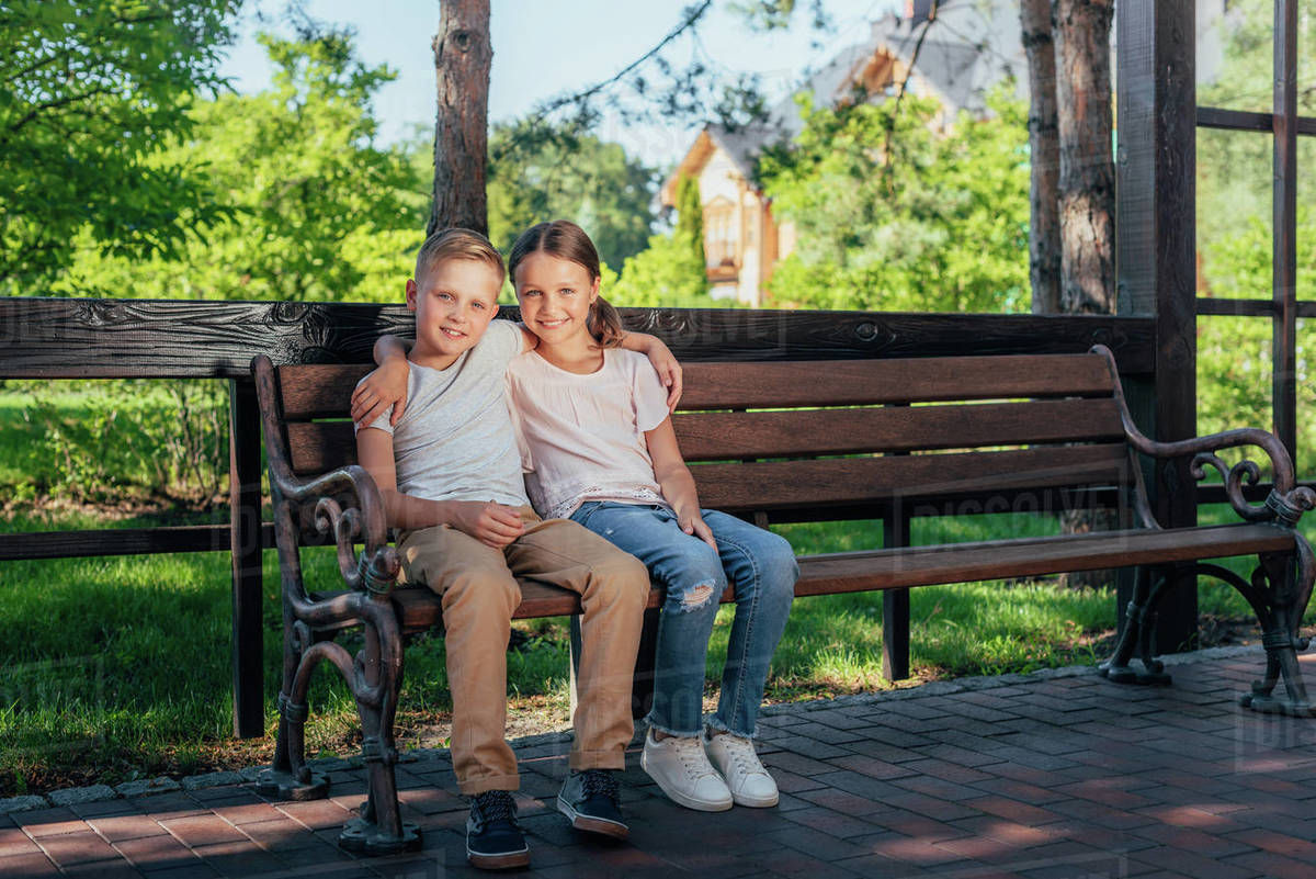 children hugging each other while sitting on bench together in park ...