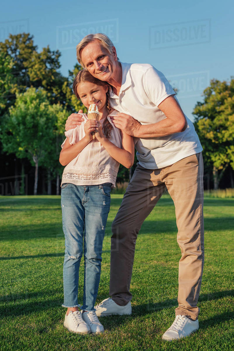 smiling senior man hugging little girl with ice cream in park - Royalty ...