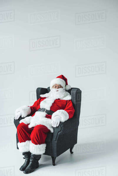 full length view of confident santa claus sitting in armchair and ...