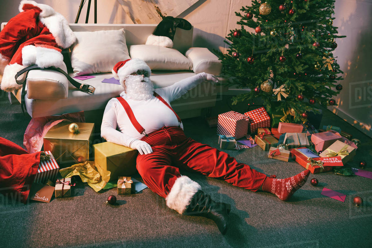 tired santa claus lying on floor in room with christmas tree and ...