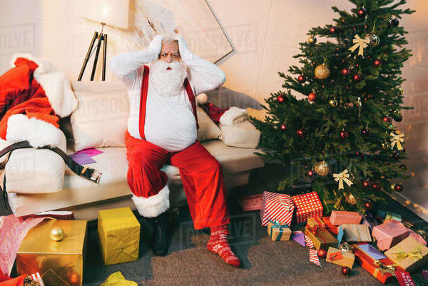 shocked santa claus sitting on sofa in room with christmas tree and ...