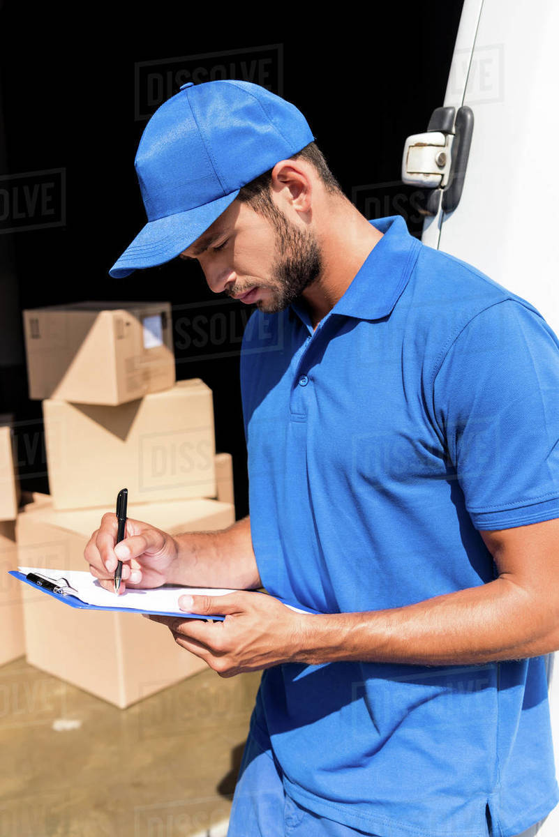Delivery man writing in documents on clipboard - Royalty-free Stock ...