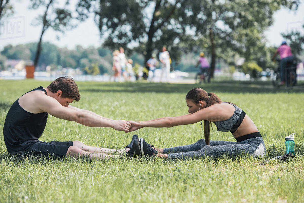 Side view of young couple in sportswear stretching together in park ...