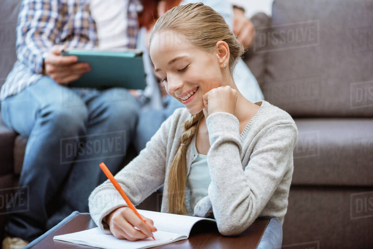 Portrait of smiling teen girl doing homework alone while parents ...