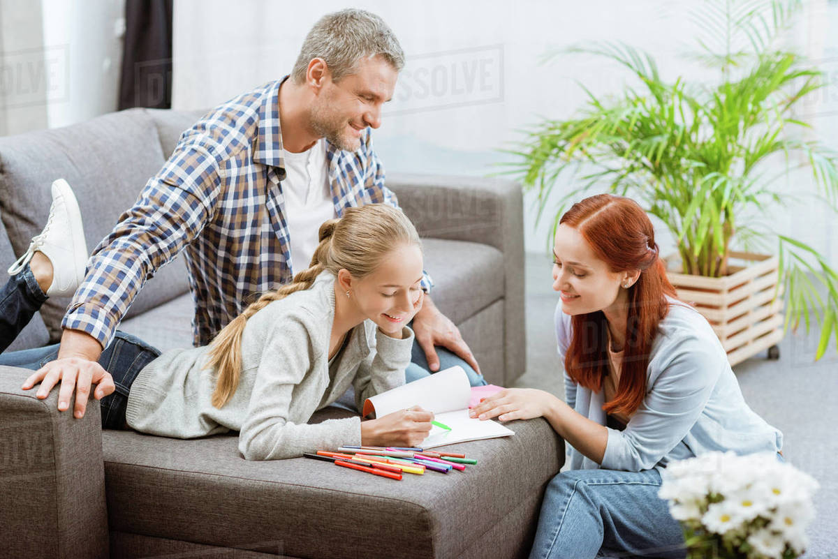 Side view of smiling parents helping teenage daughter with homework at ...