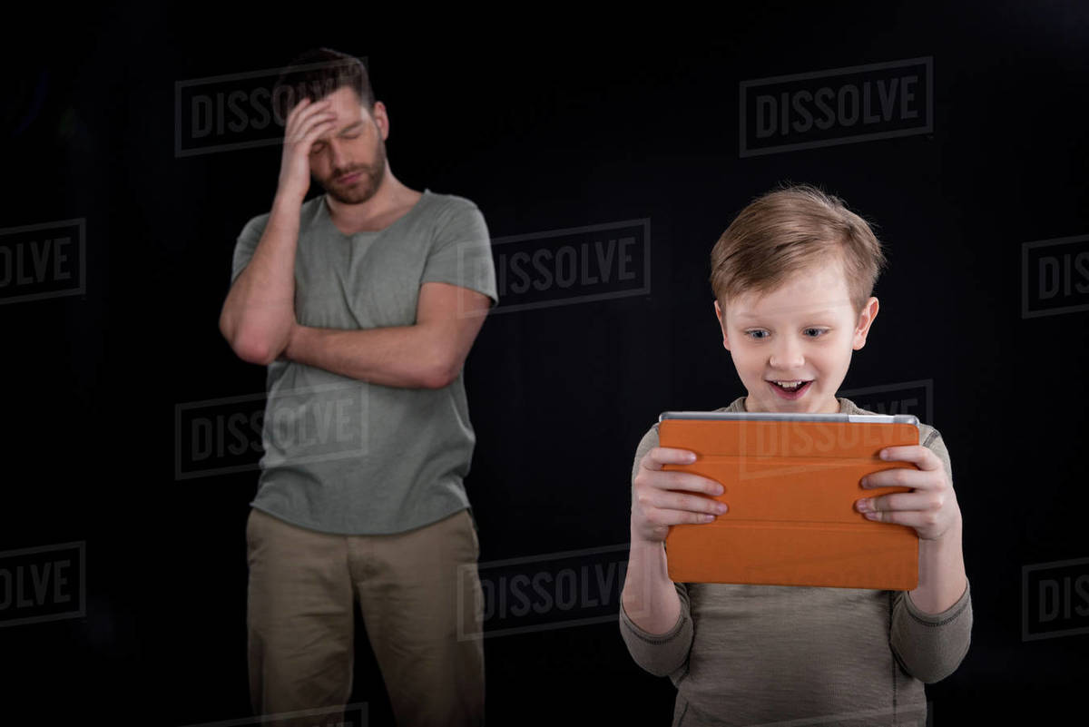 Upset father standing behind excited son using digital tablet, family ...