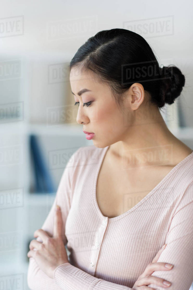 Portrait of pensive young asian woman standing with crossed arms and ...