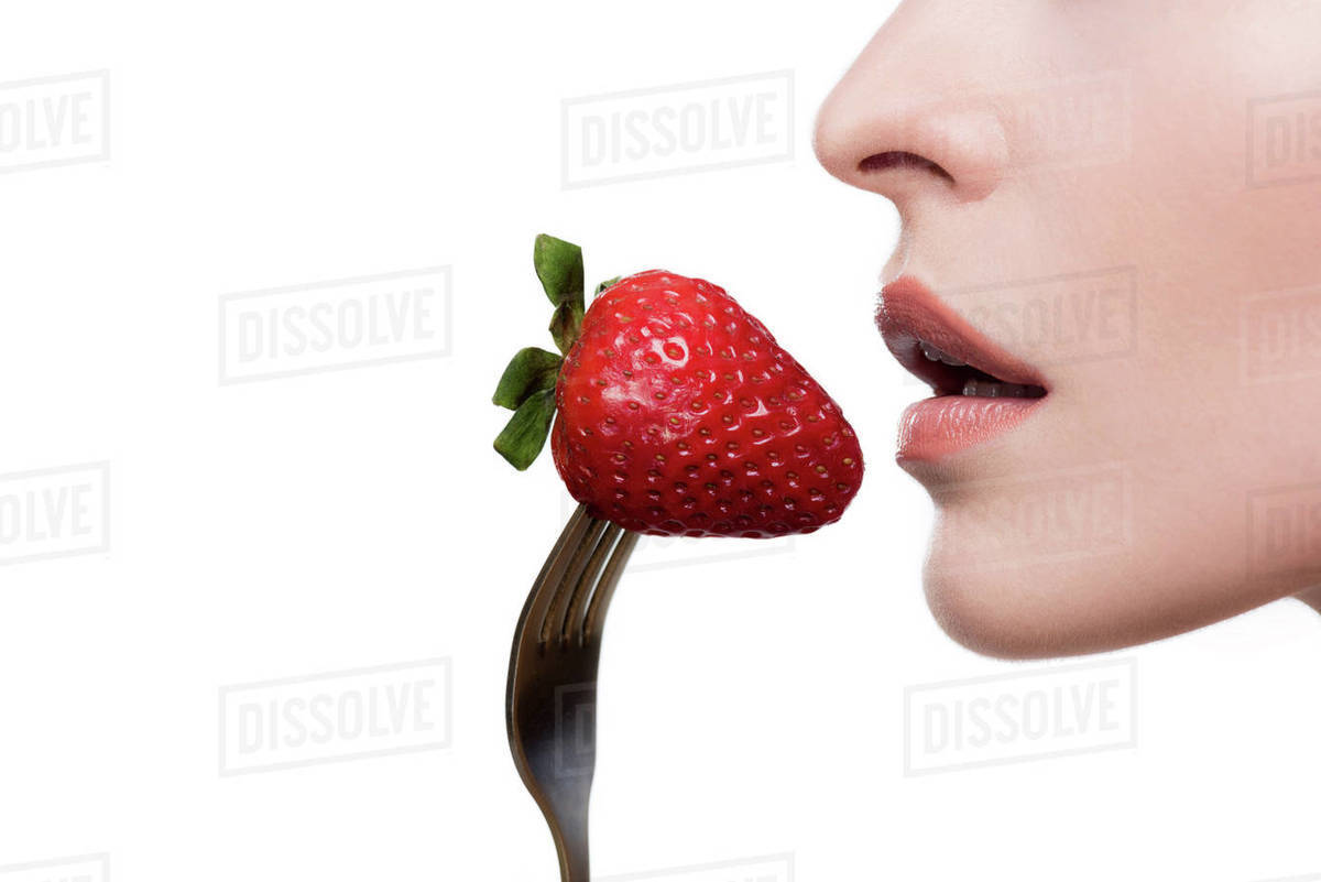 Cropped shot of young woman eating strawberry on fork isolated on white ...
