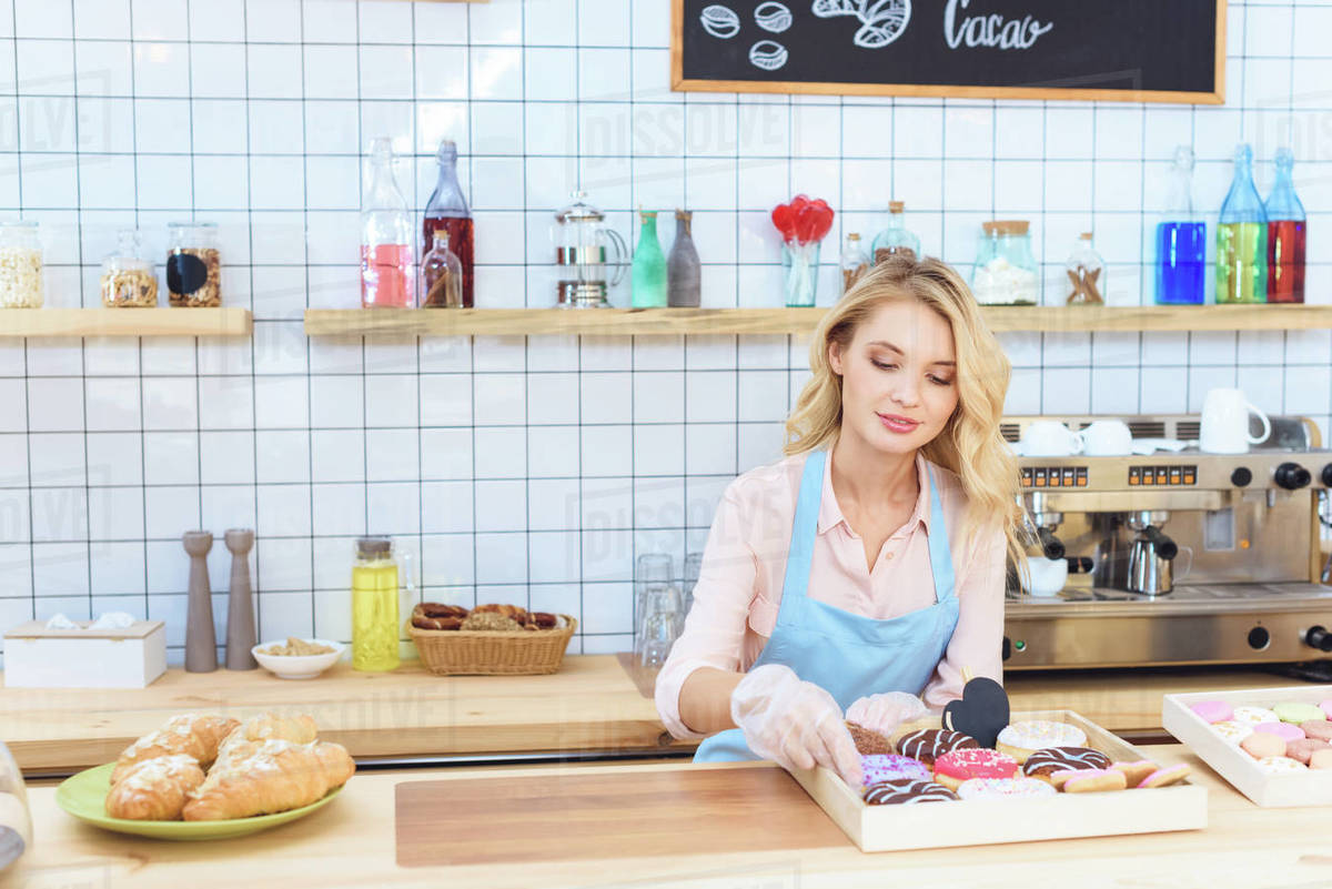 Beautiful smiling young waitress putting delicious donuts in box ...