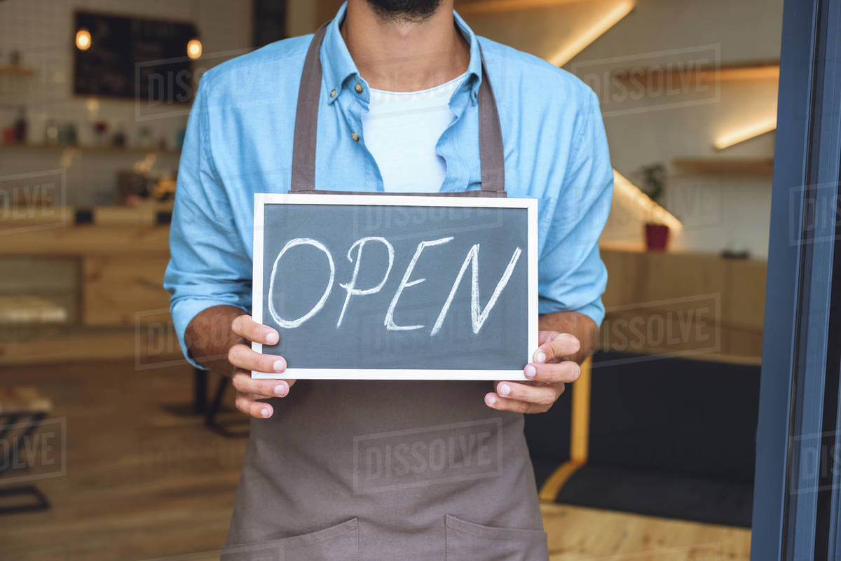 Cropped shot of waiter in apron holding sign open - Stock Photo - Dissolve