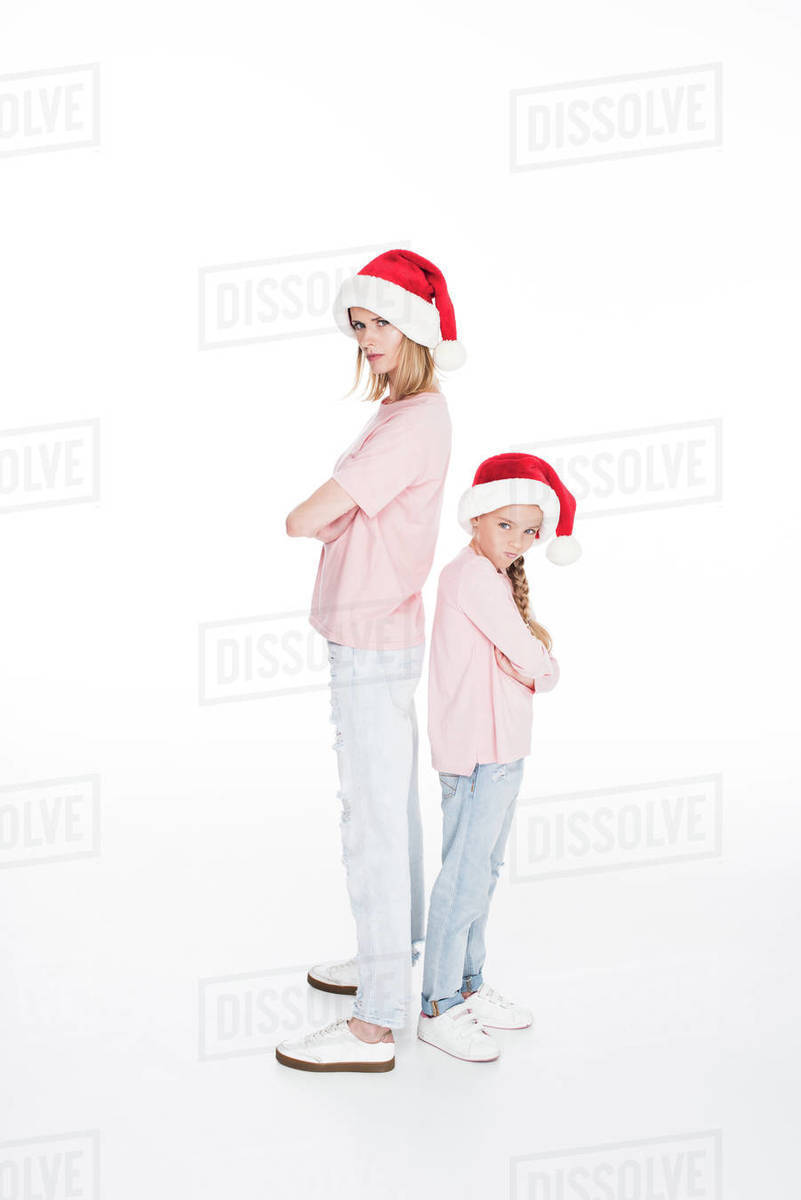 Grumpy mother and little daughter in Santa hats posing with arms ...