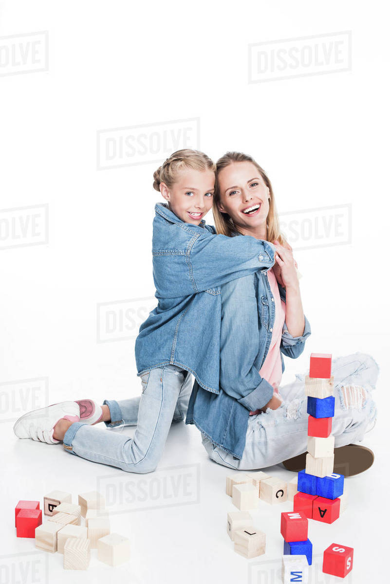 Daughter hugging mother from behind while they're sitting on floor with ...