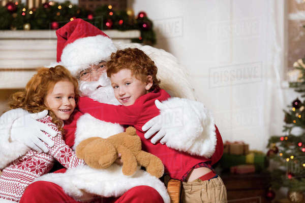 Portrait of smiling kids hugging Santa Claus at home - Royalty-free ...