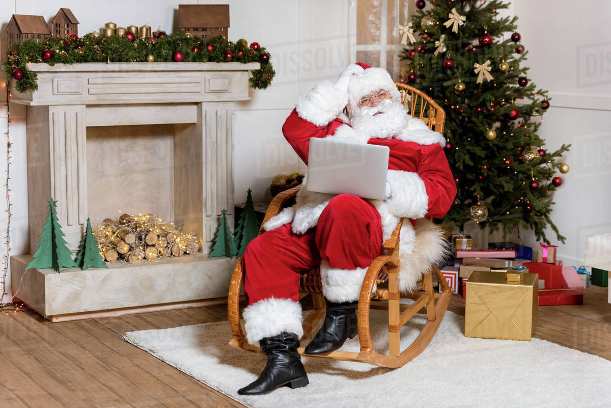 Pensive Santa Claus with laptop resting on rocking chair at home ...