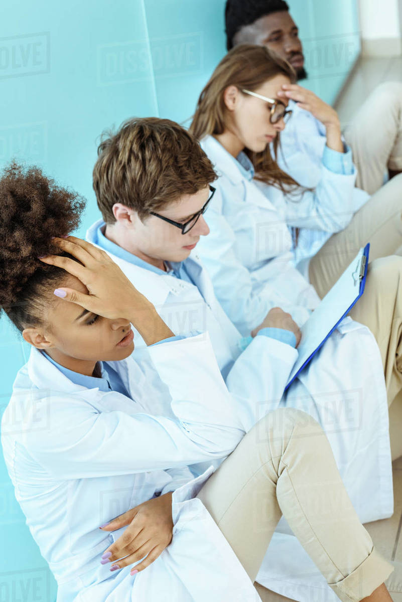 Four young medical interns in white robes sitting on a floor in ...