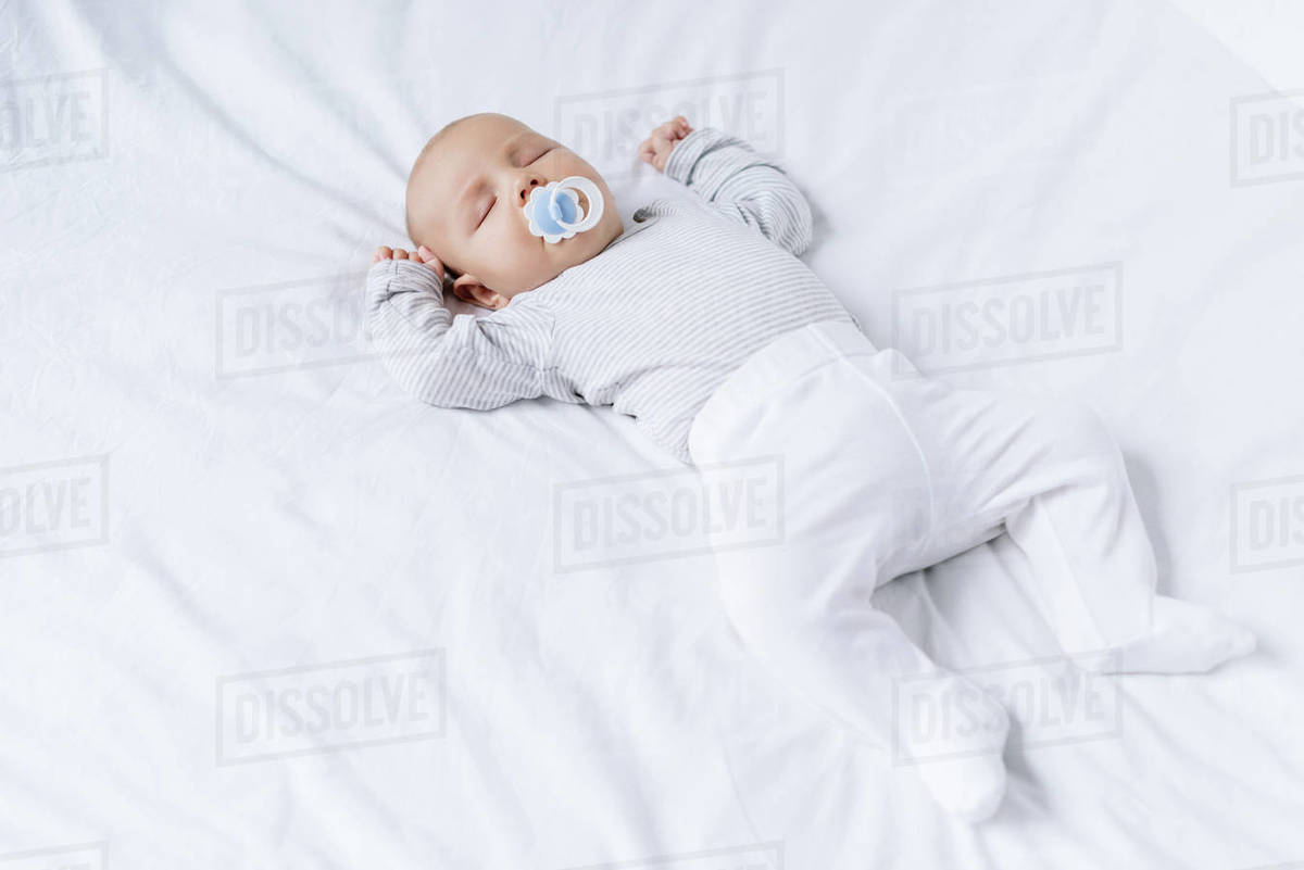 Overhead view of baby with pacifier in mouth sleeping on bed - Royalty ...