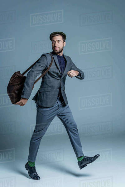 Young man in suit and flat cap, walking with leather bag on his ...