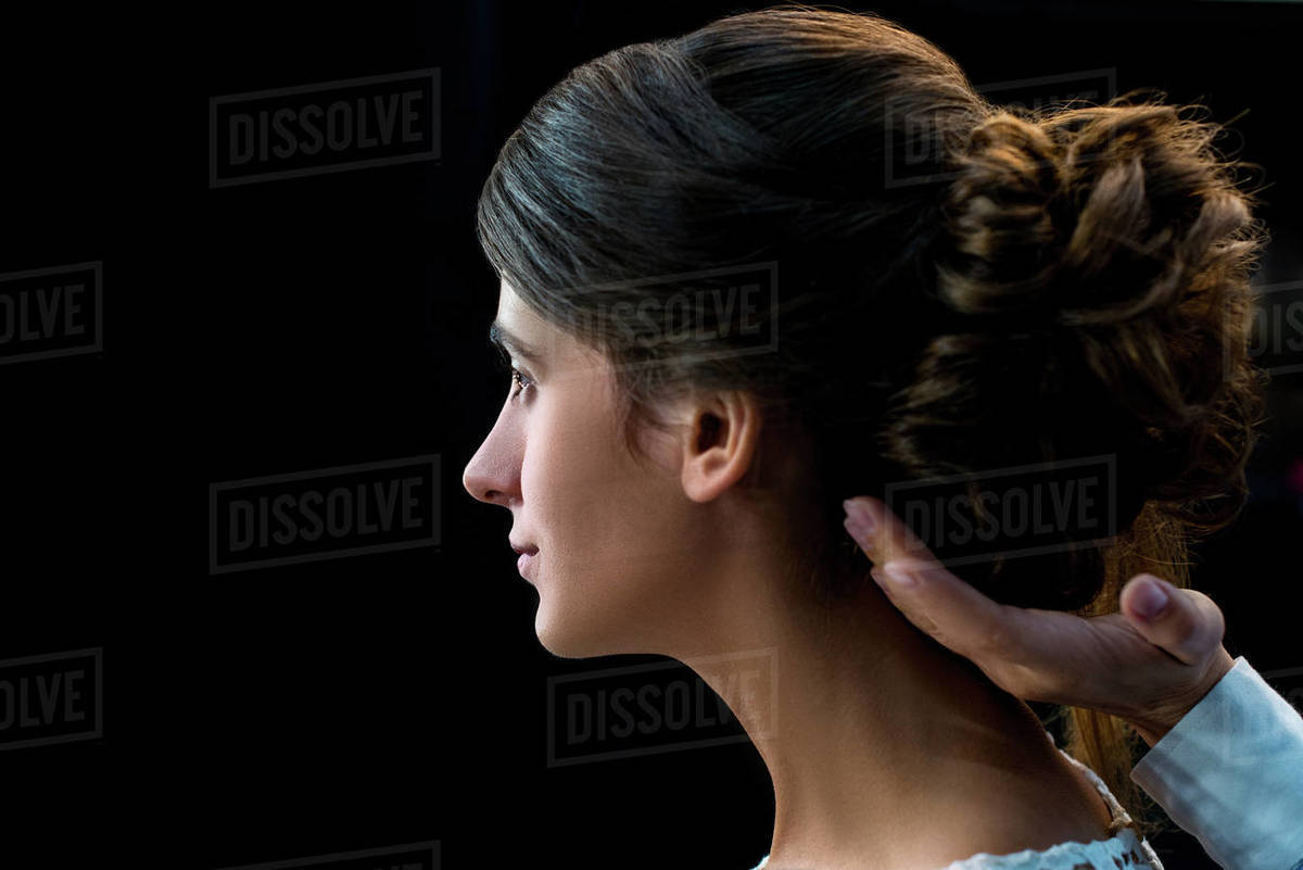 Side view of woman getting hair done by hairstylist isolated on black ...