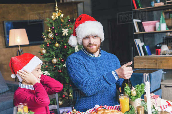 Handsome father and son in Santa hats opening champagne bottle on ...