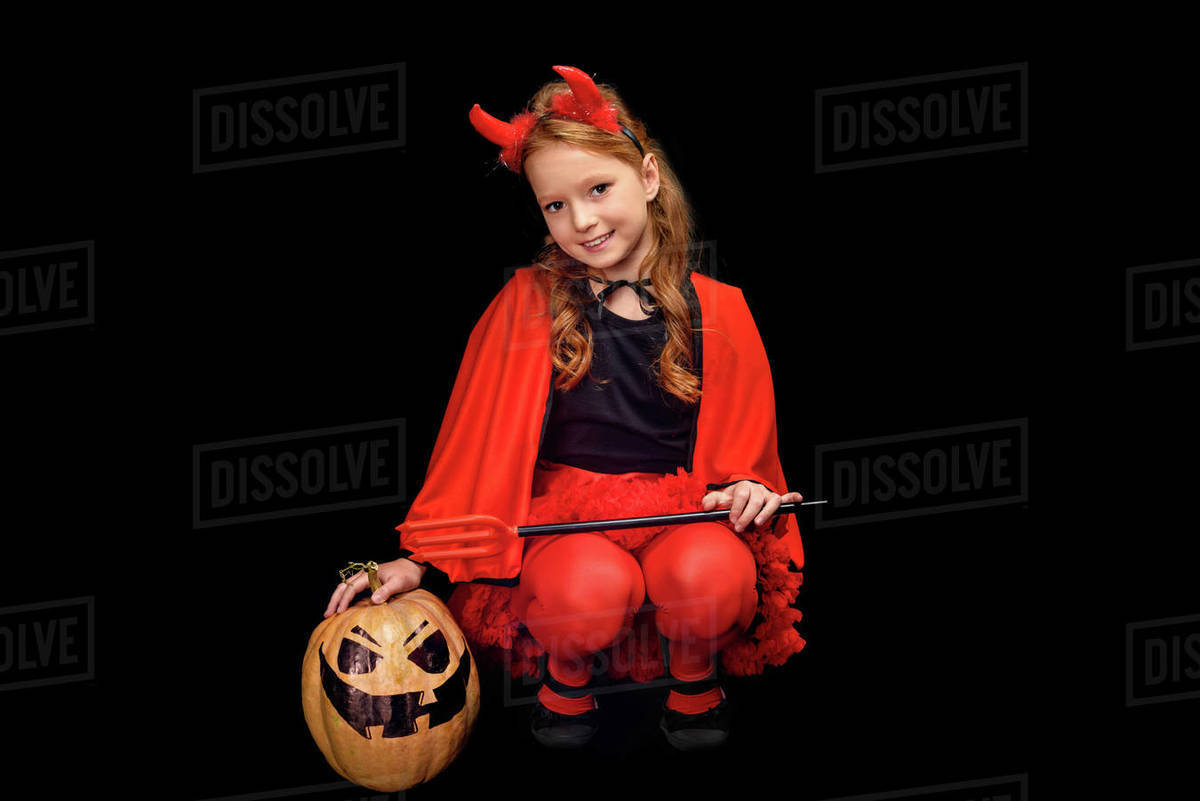 Child in Halloween costume of devil with pitchfork and pumpkin jack o ...