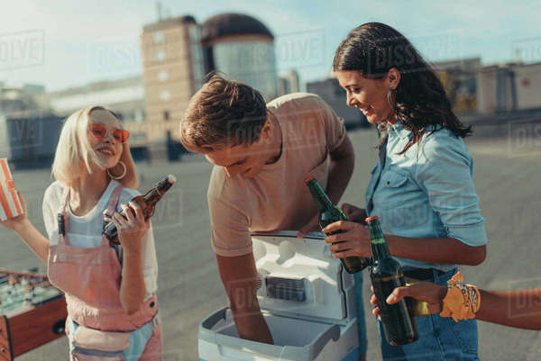 Group of young friends sharing beer from portable fridge for roof party ...