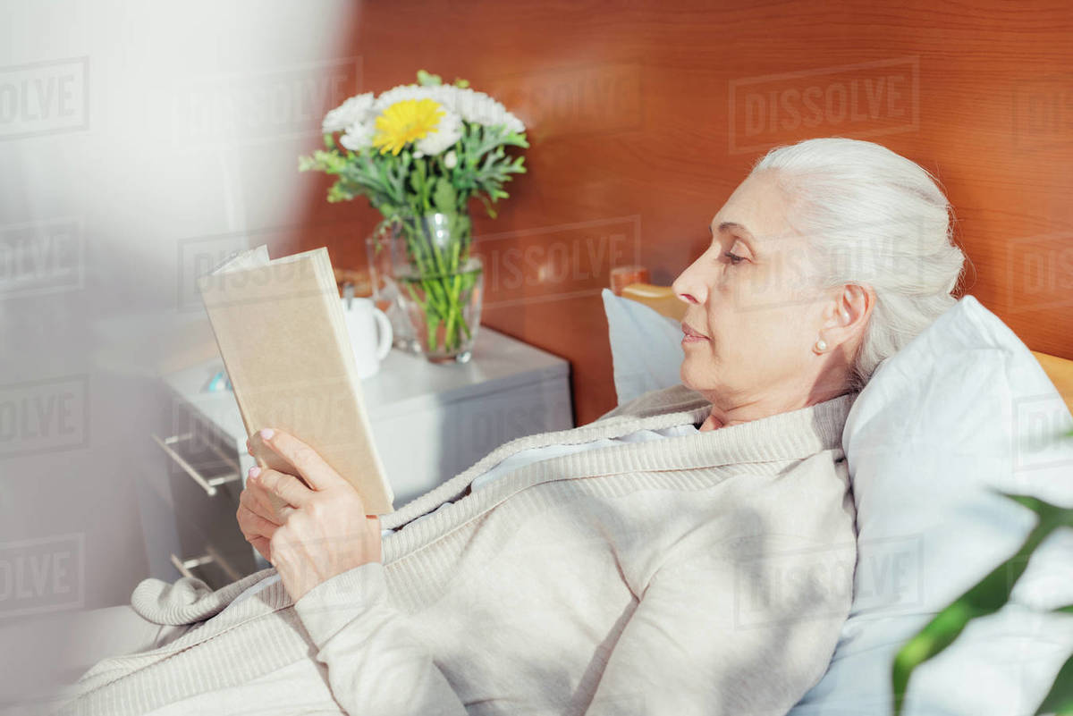 side view of senior woman reading book in hospital - Stock Photo - Dissolve