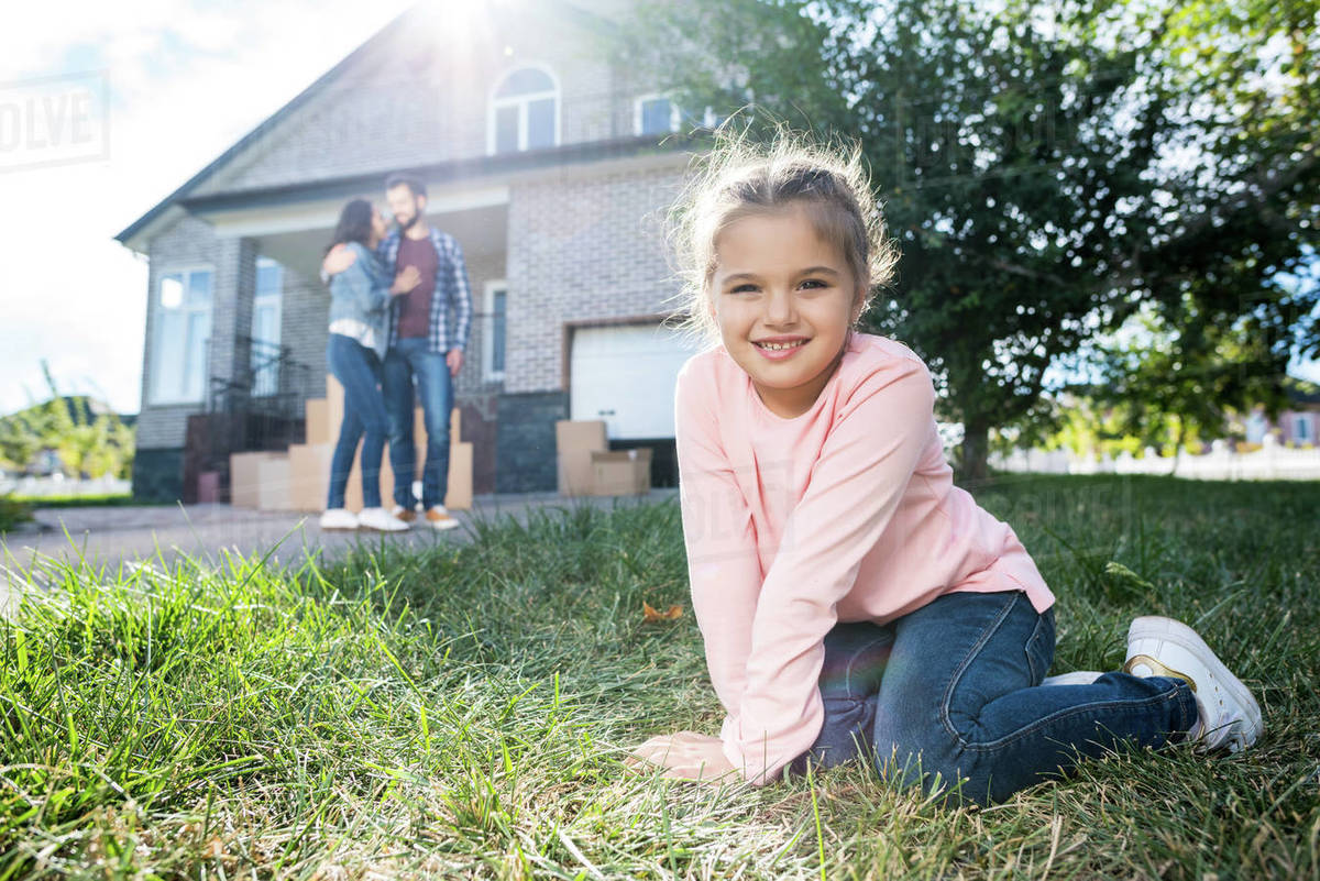 Girl sitting in garded of new house while parents embracing on ...