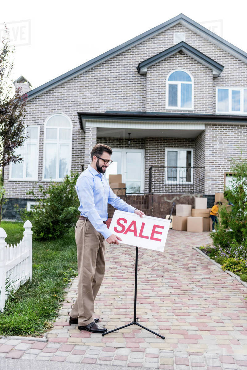 Handsome young realtor with sale signboard in front of house - Stock ...