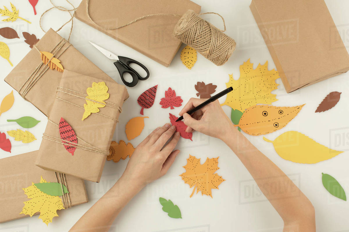 Cropped shot of female hands handcrafting paper leave for autumn gifts ...