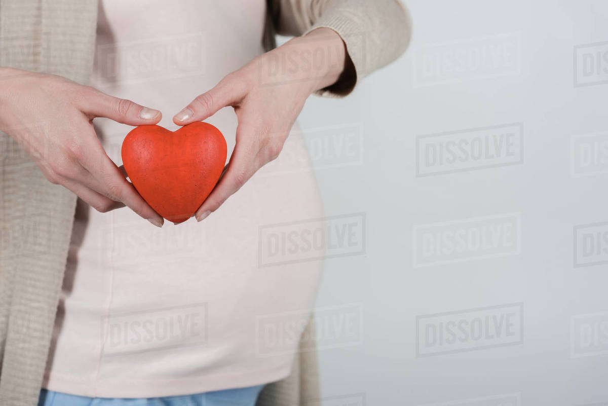 Close-up, cropped image of pregnant woman's belly and heart in hands ...