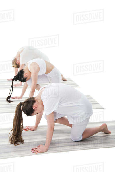 Women performing knee to forehead asana or eka pada marjariasana on ...