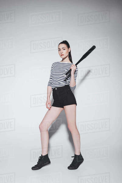 Beautiful young confident woman holding baseball bat and posing on grey ...