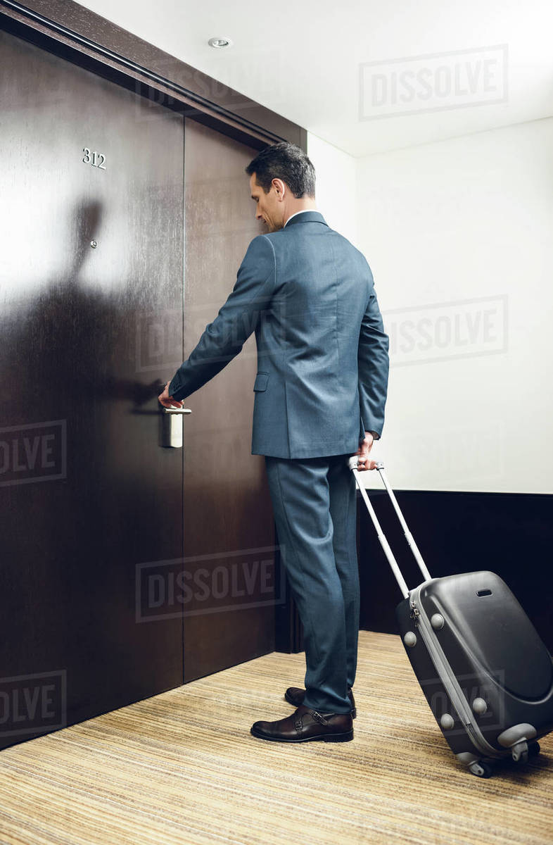 Businessman in formal suit holding a suitcase and opening hotel room ...