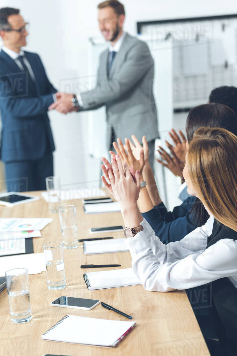 Boss shaking hand of manager while colleagues clapping at conference ...
