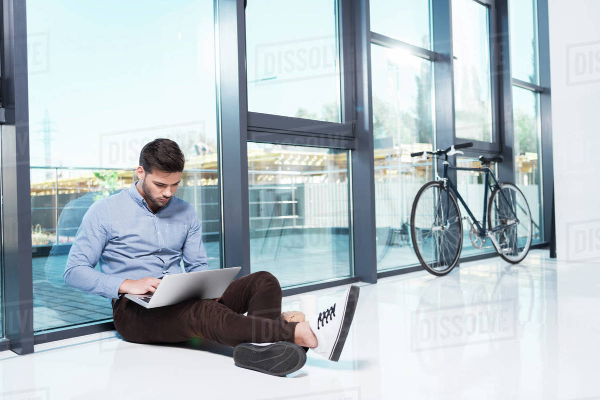 Handsome young businessman using laptop while sitting on floor in office - Royalty-free Stock ...