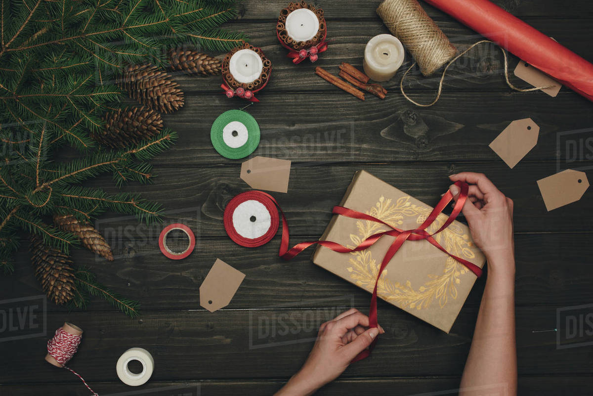 Top view of woman tying up bow of red ribbon on christmas gift ...