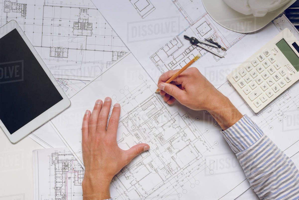 partial view of architect working with blueprints on new building ...