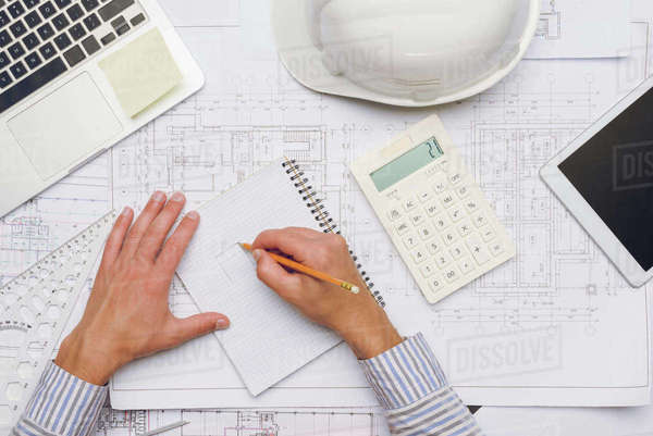 cropped shot of architect writing in notebook while working on ...