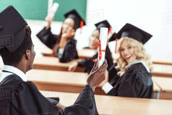happy multiethnic students in graduation costumes showing diplomas ...