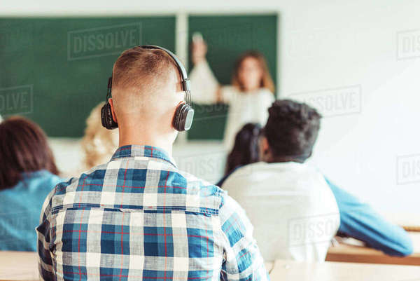 back view of student listening music with headphones on lecture ...
