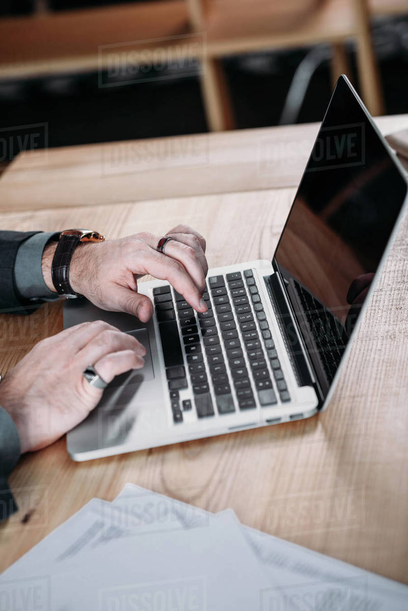 Close-up partial view of businessman typing on laptop with blank screen ...