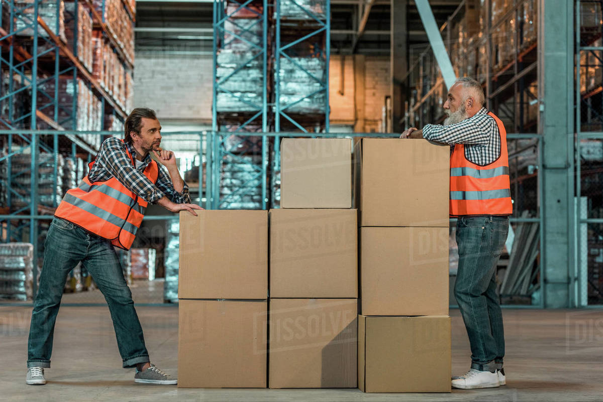 Full length view of two male warehouse workers standing with boxes and ...