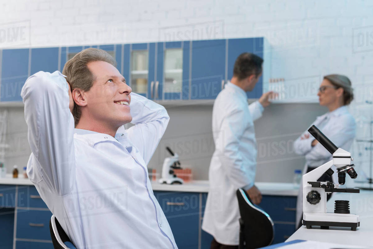 Smiling medical worker in laboratory, sitting with arms behind neck ...