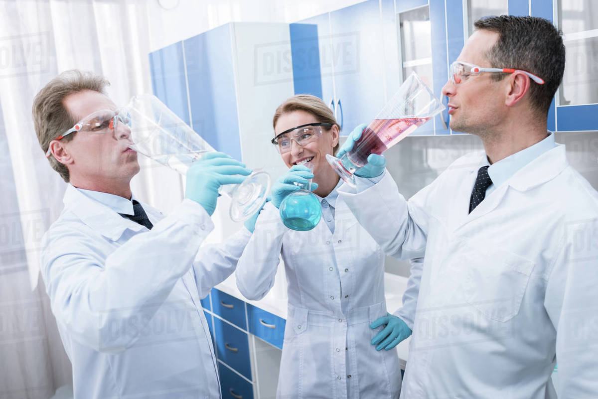 A team of smiling doctors in lab coats pretending to drink from test ...